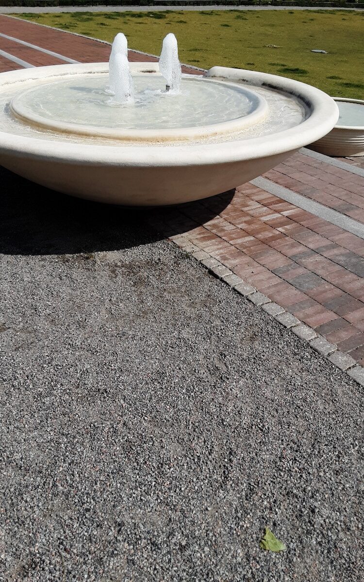 Round small fountain in a park summertime with gravel around base ...
